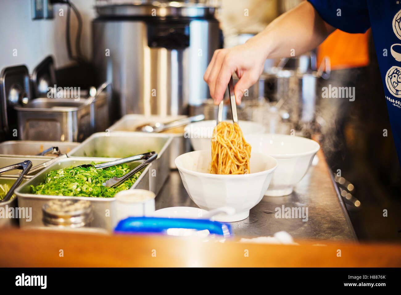 A ramen noodle shop kitchen. A chef preparing bowls of ramen noodles in ...