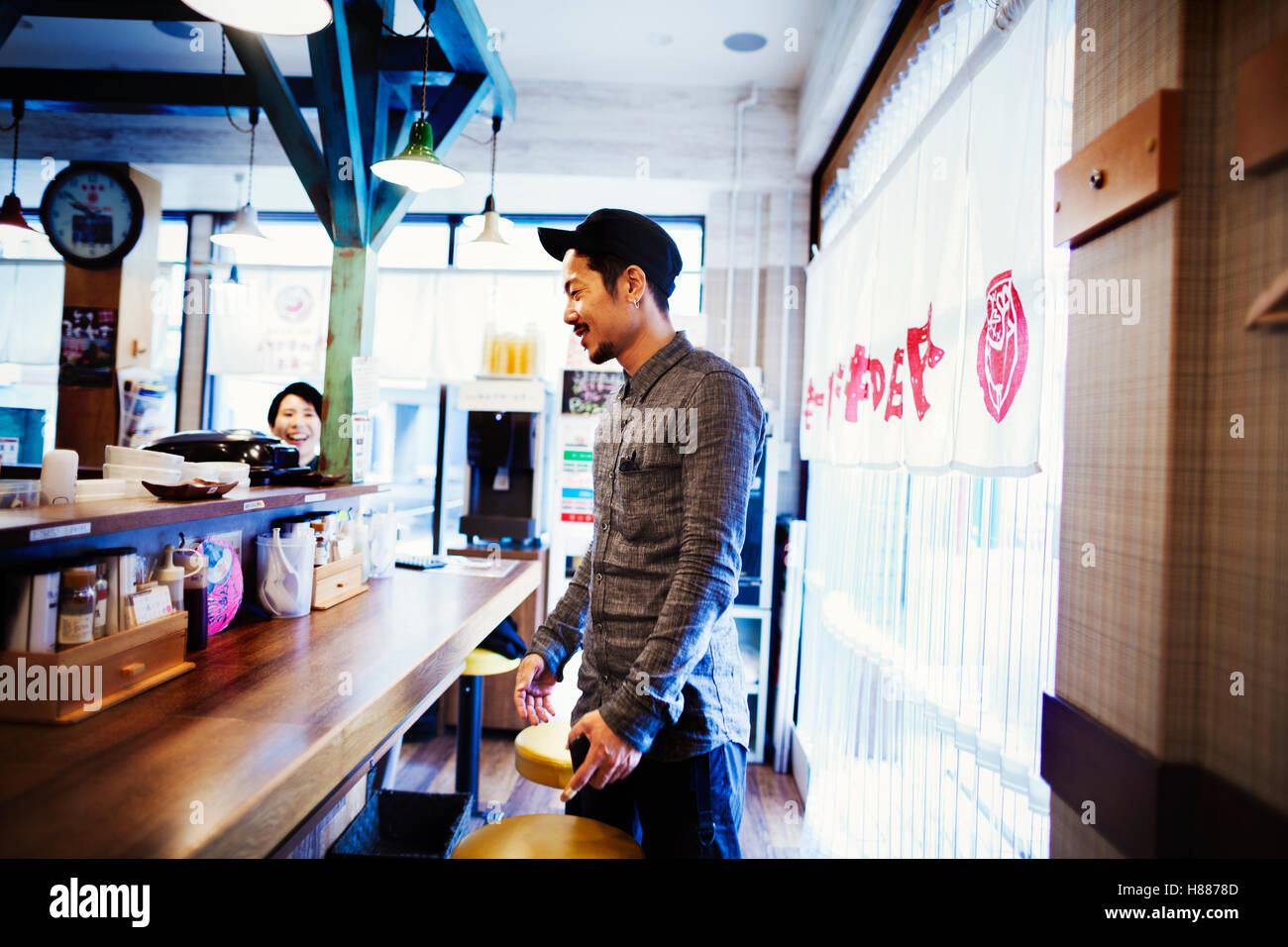 A ramen noodle cafe in a city. Customer standing up at the counter ...