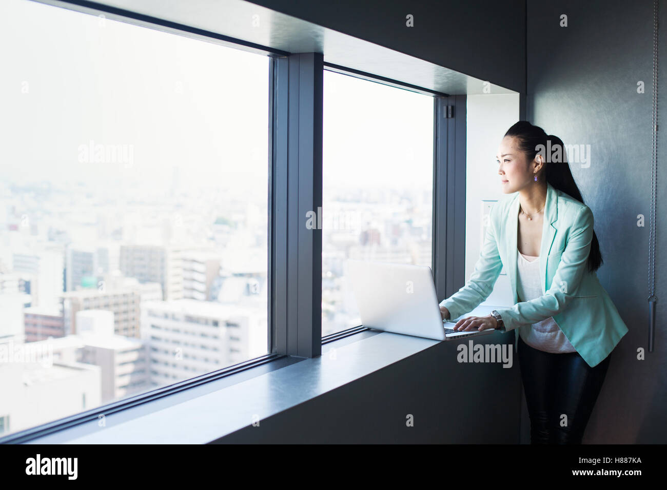 A business woman by a window with a view over the city, looking out ...