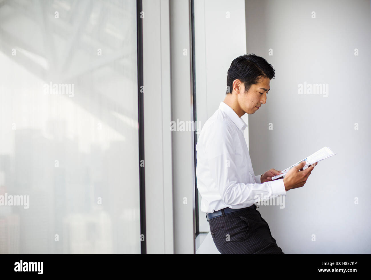 A businessman in the office, by a large window reading paperwork ...