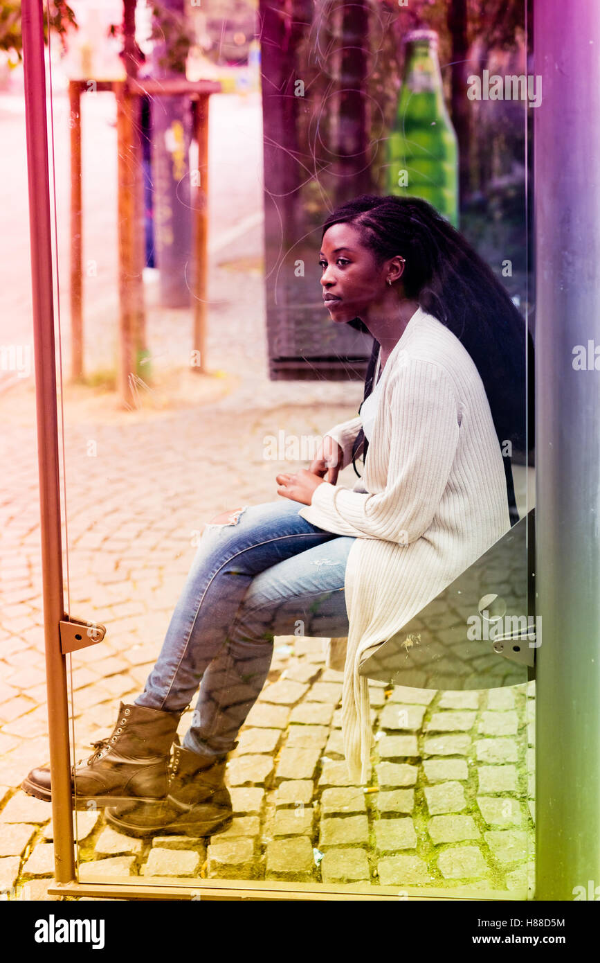 Young beautiful black woman sitting at the bus stop, overlooking ...