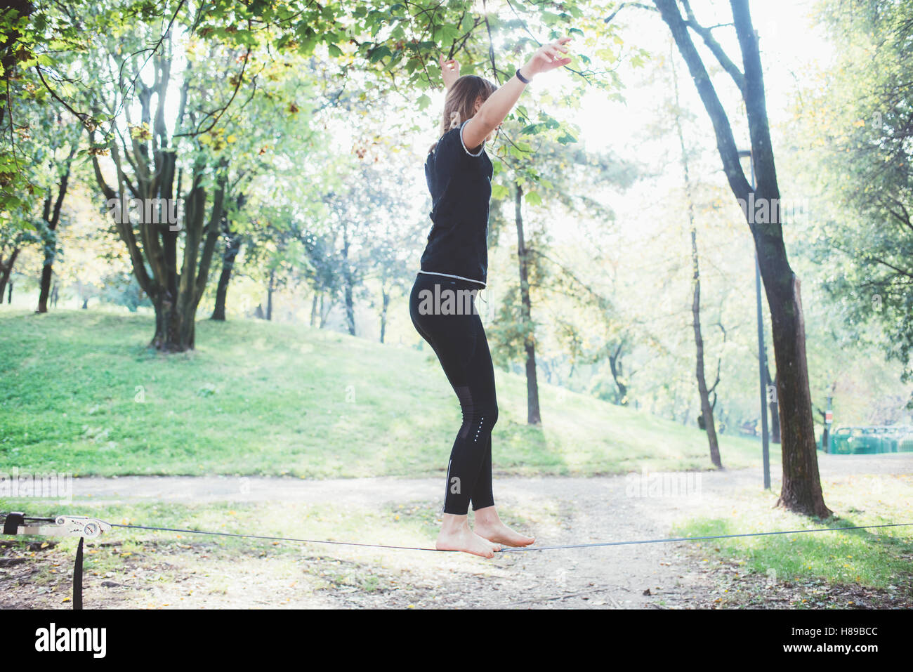 Woman balancing a tightrope or slackline outdoor in a city park in ...