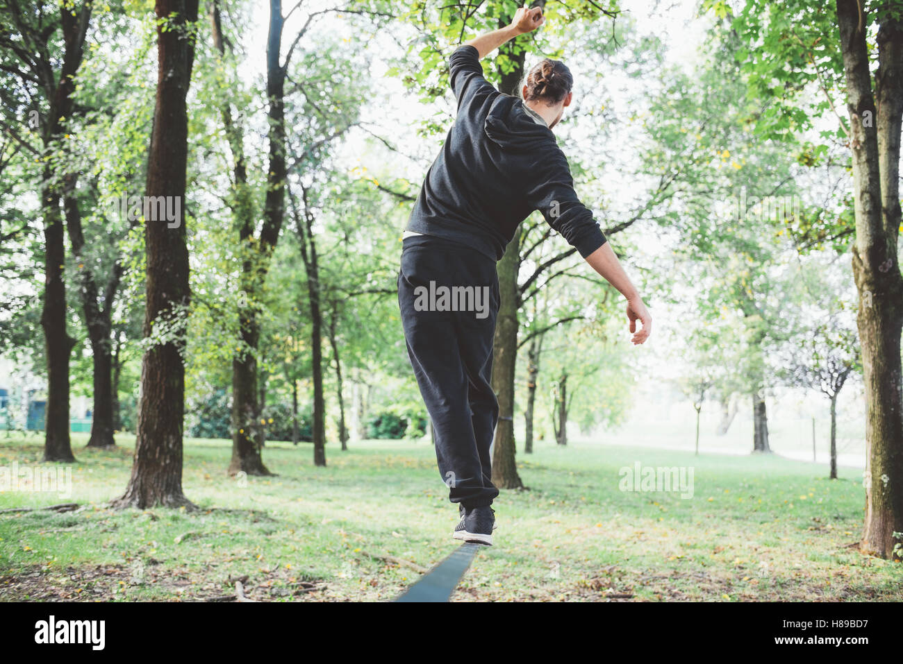 Man balancing a tightrope or slackline outdoor in a city park in autumn ...