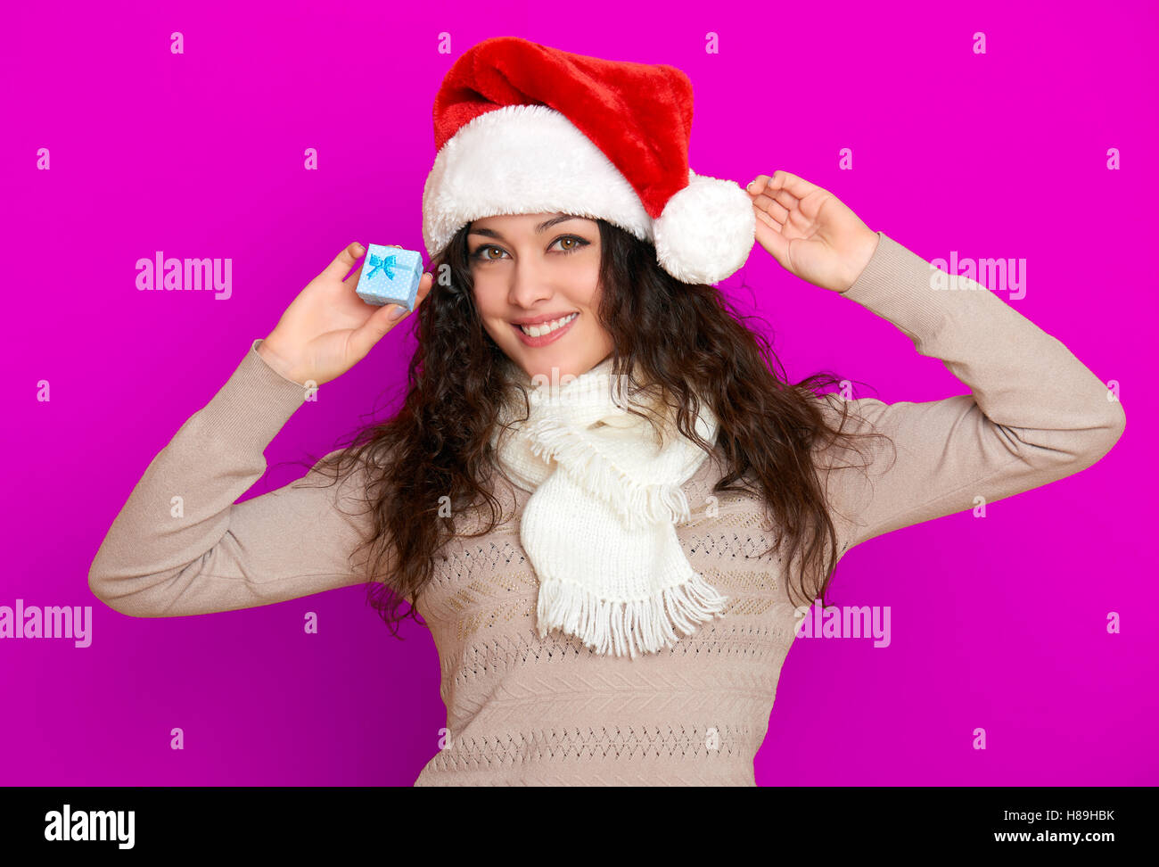 girl in santa hat portrait with little gift box posing on pink color ...