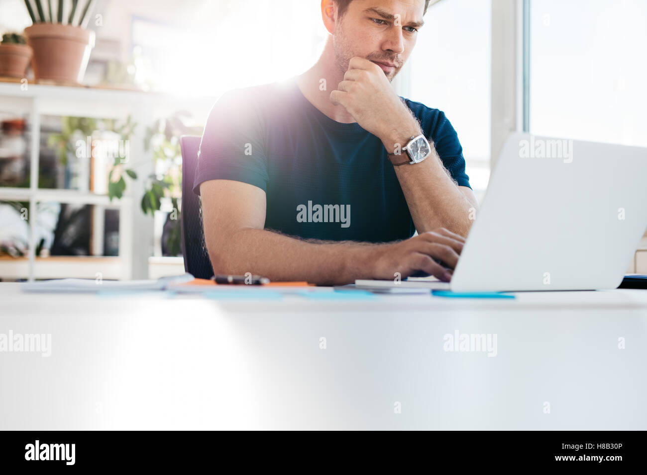 Indoor shot of young man sitting at a table and working on laptop ...