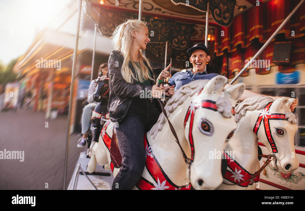 Smiling man and woman on amusement park carousel. Young couple on horse ...