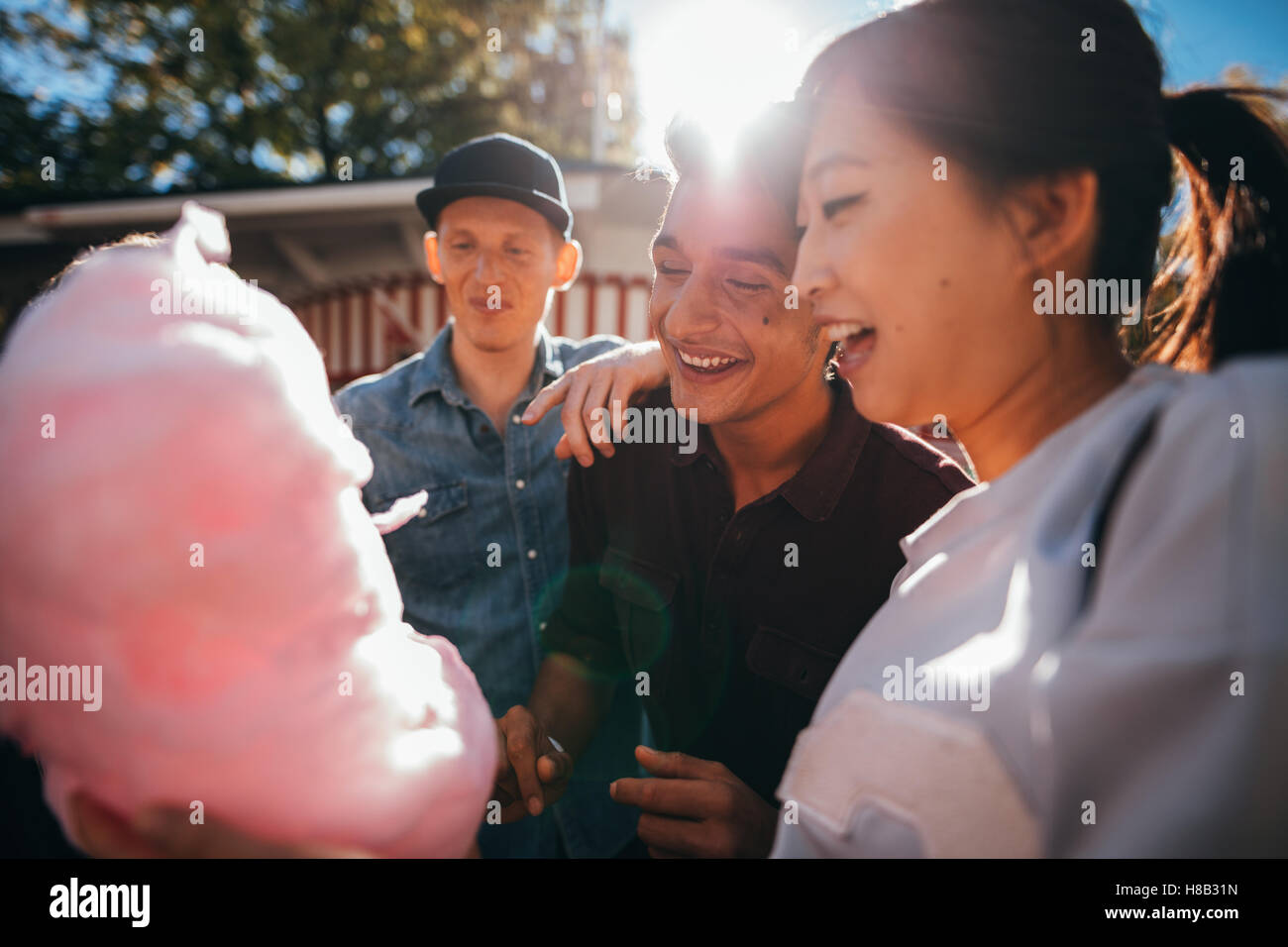 Three friends eating candy floss at amusement part. Young men and woman ...