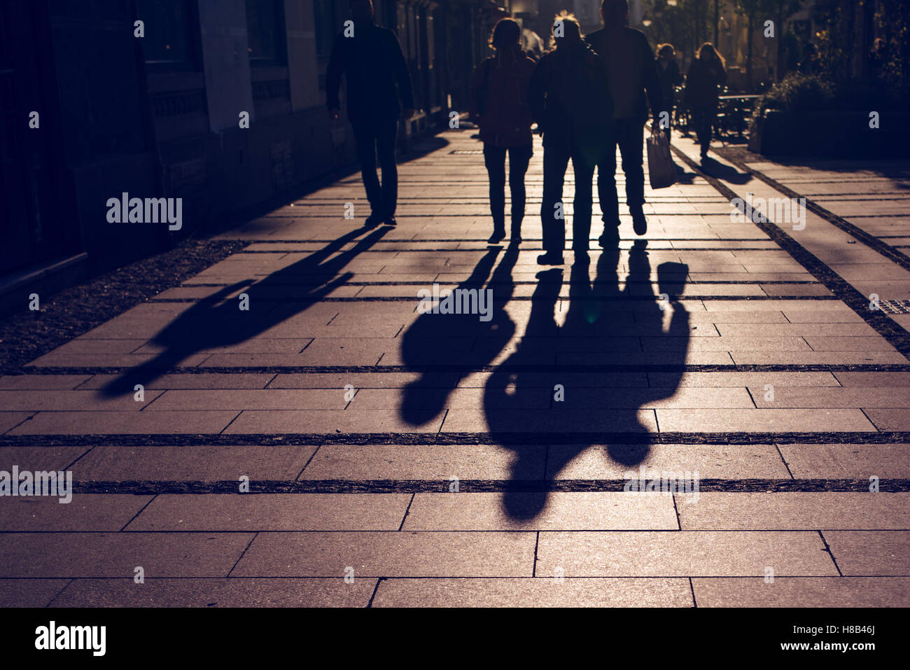 Silhouettes of people walking on city street and casting shadows on ...