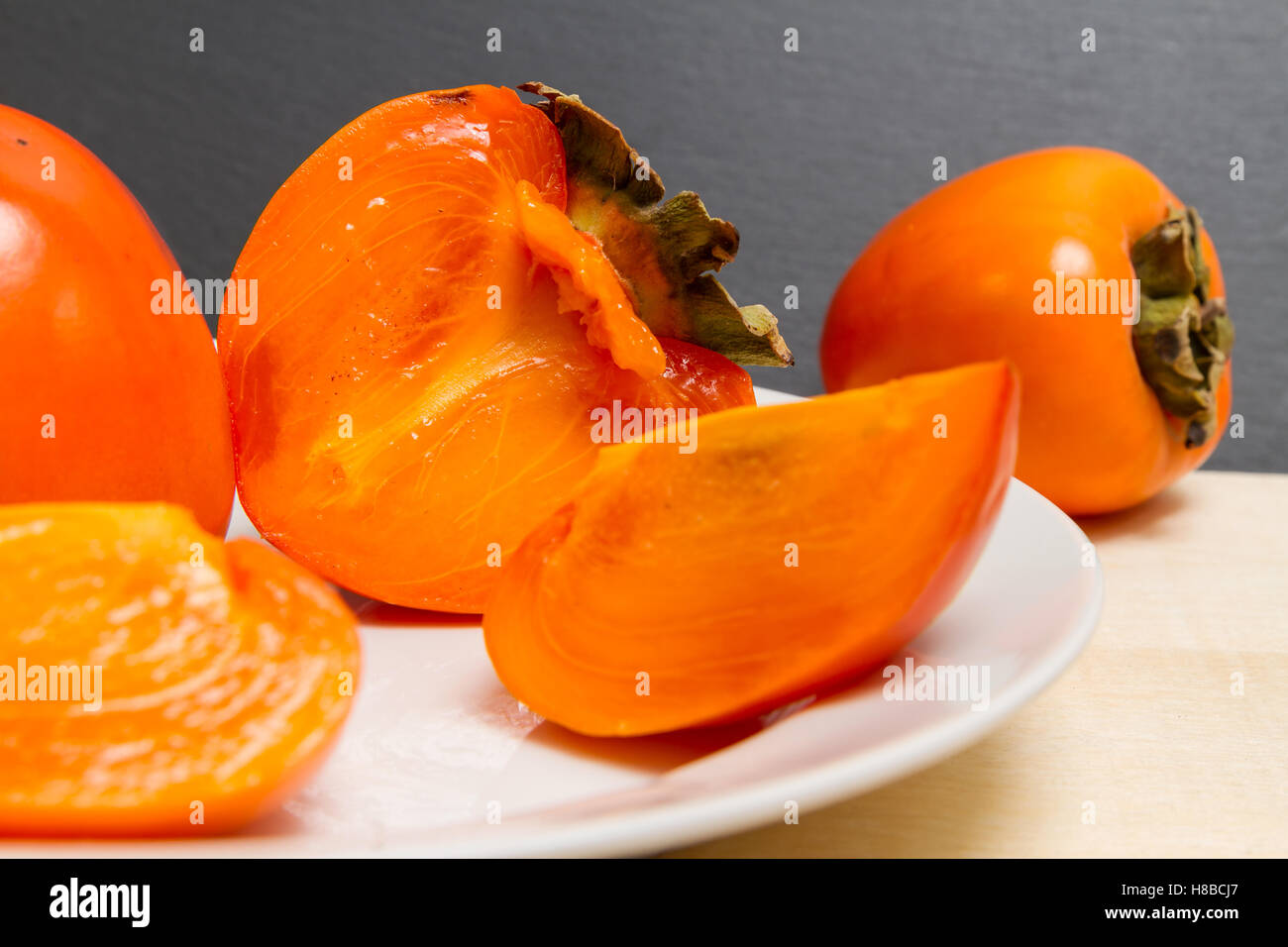 Cut a ripe persimmon on a white plate Stock Photo - Alamy
