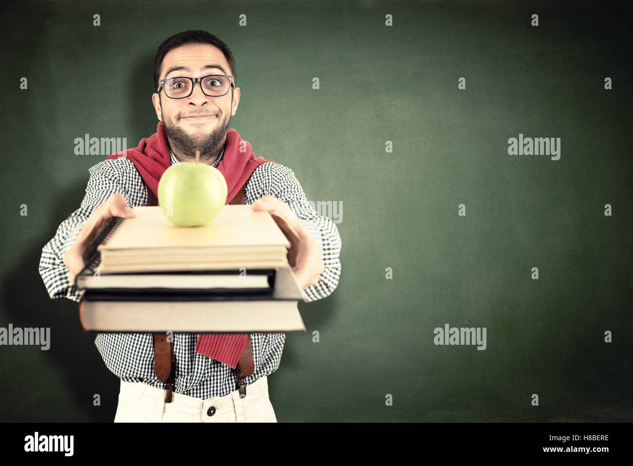 Nerd student posing with books and apple against a chalk board Stock ...