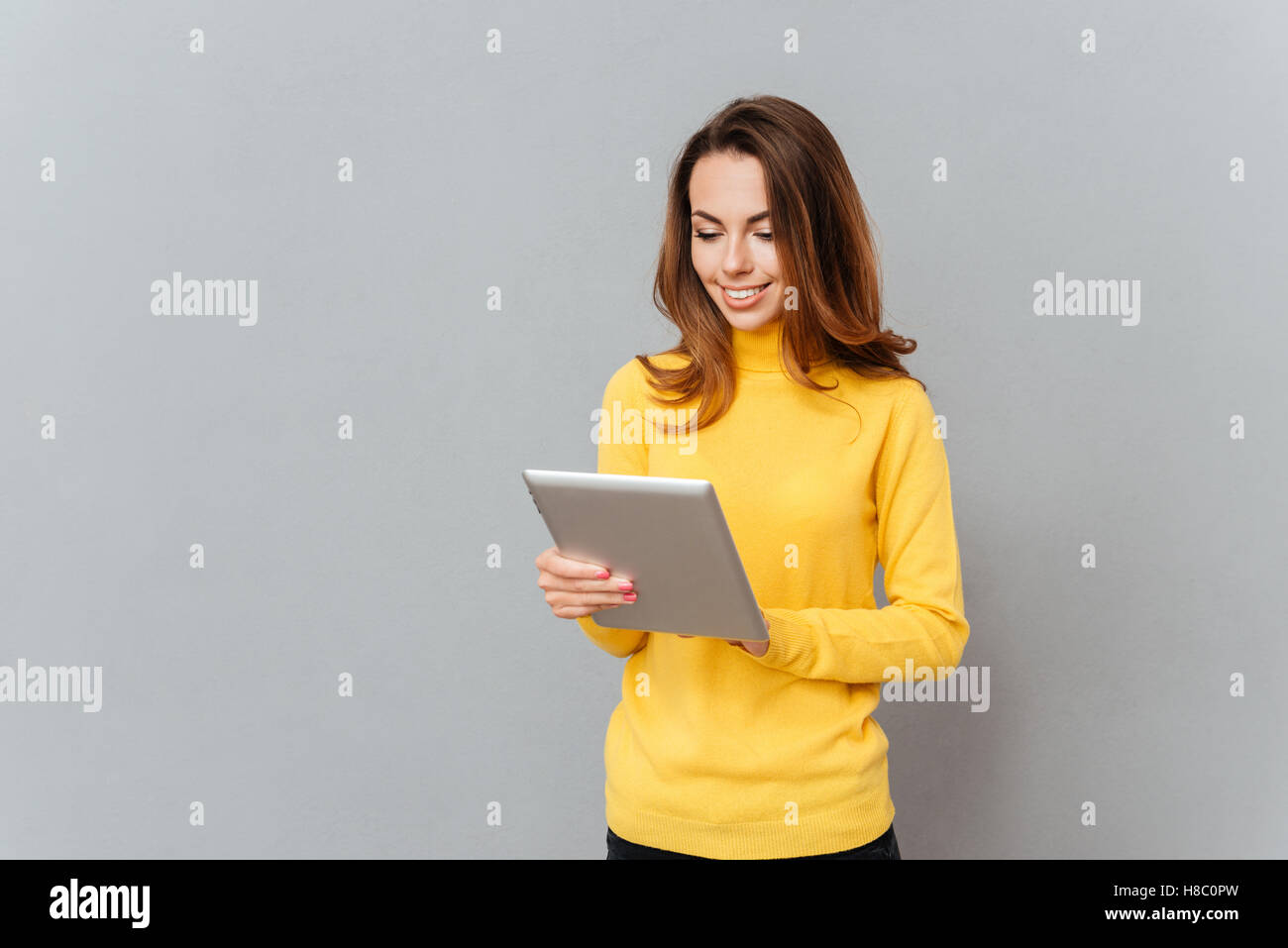Smiling young woman in yellow sweater using tablet computer isolated on ...
