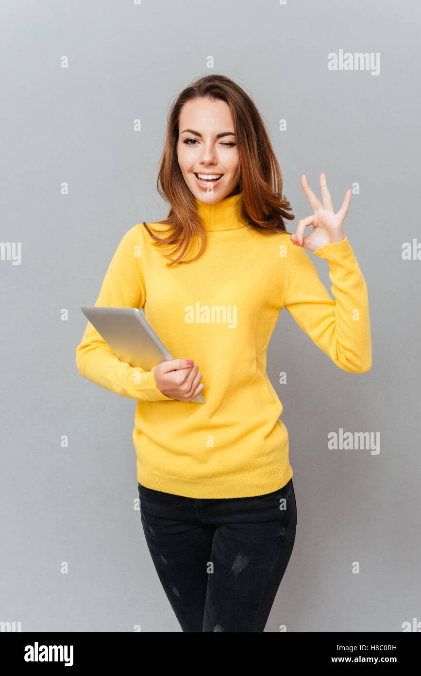 Happy casual woman with tablet computer winking and showing ok sign ...