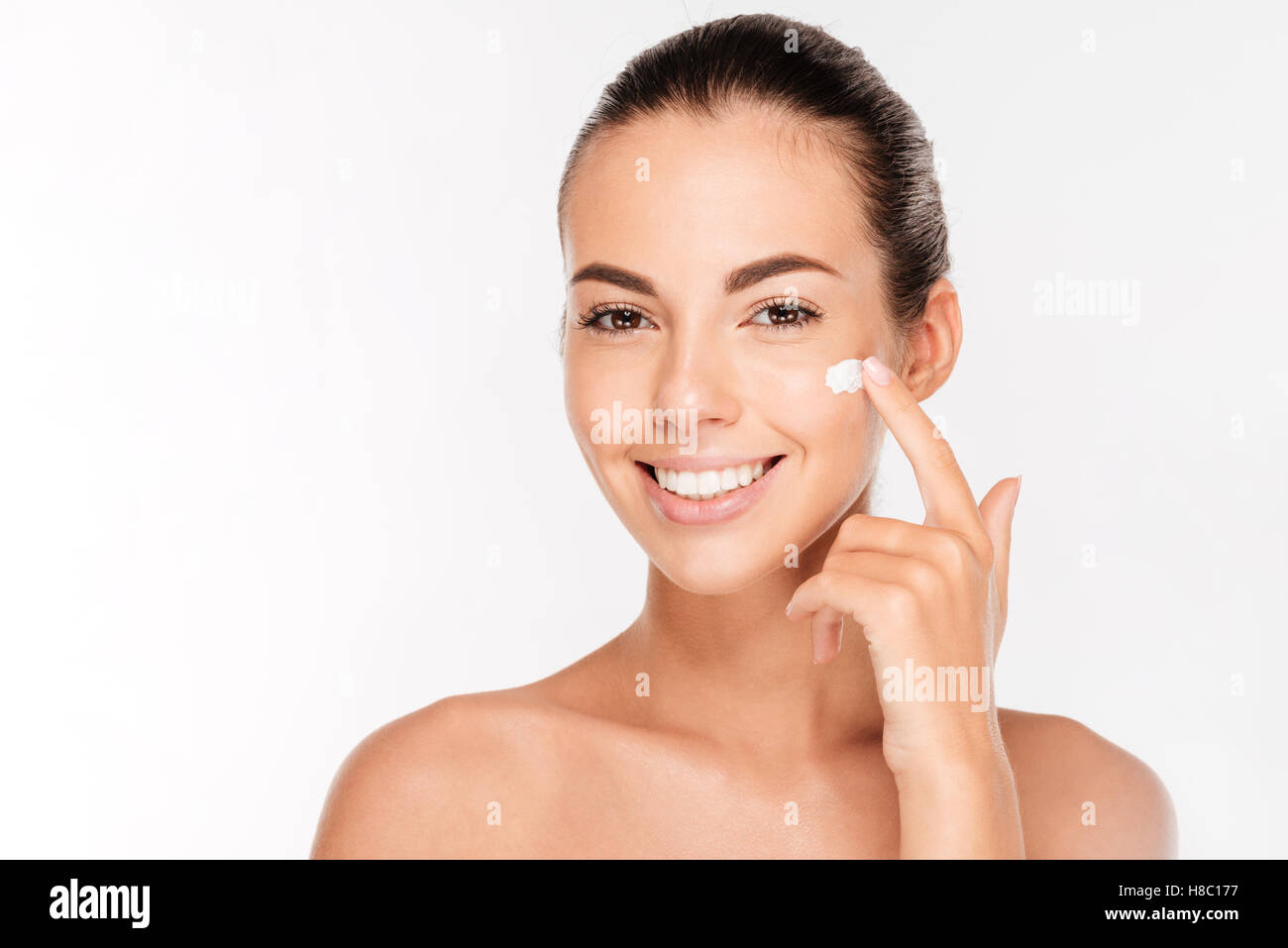 Beautiful young woman applying cosmetic cream treatment on her face isolated on white background ...