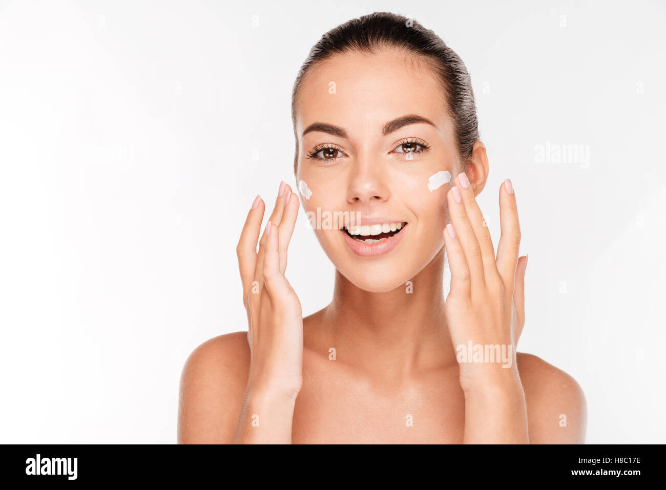 Beautiful young woman applying cosmetic cream treatment on her face isolated on white background ...