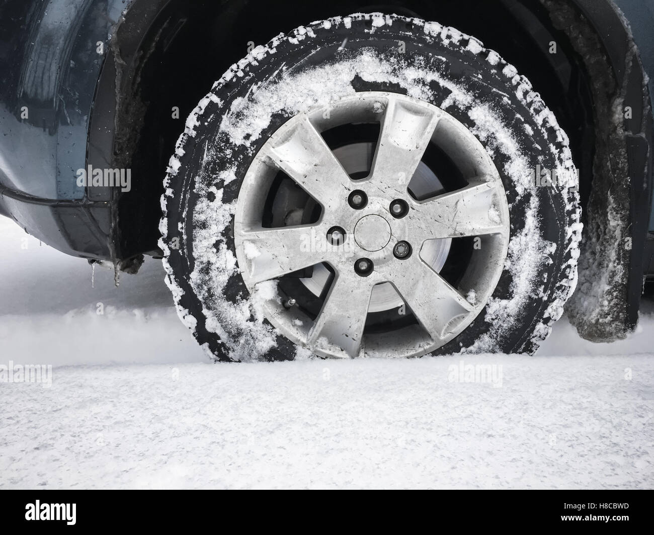 Modern car wheel with studded tire stands on winter road with deep snow ...