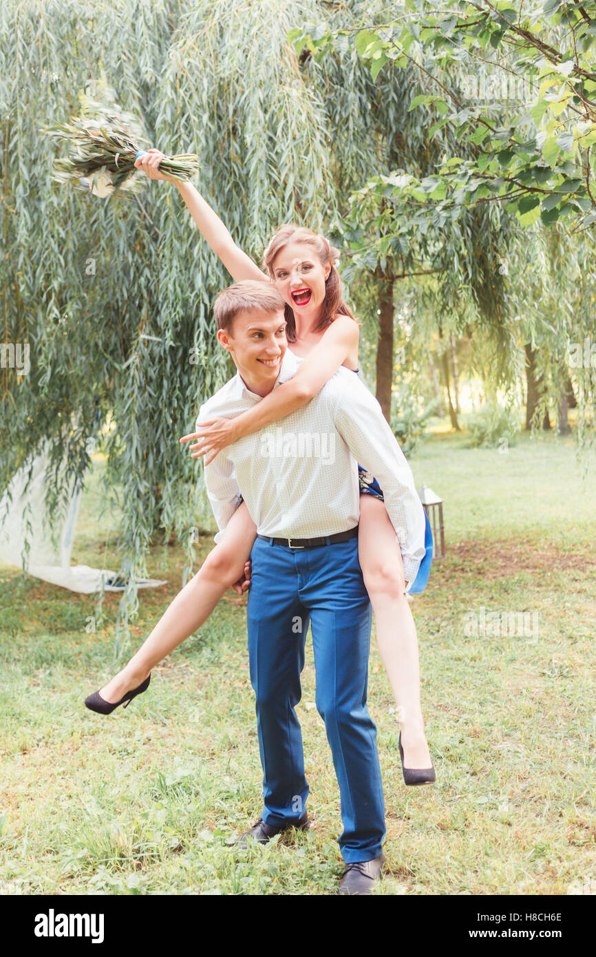 Happy young couple, she jumped on his back, in the park. Holding a ...