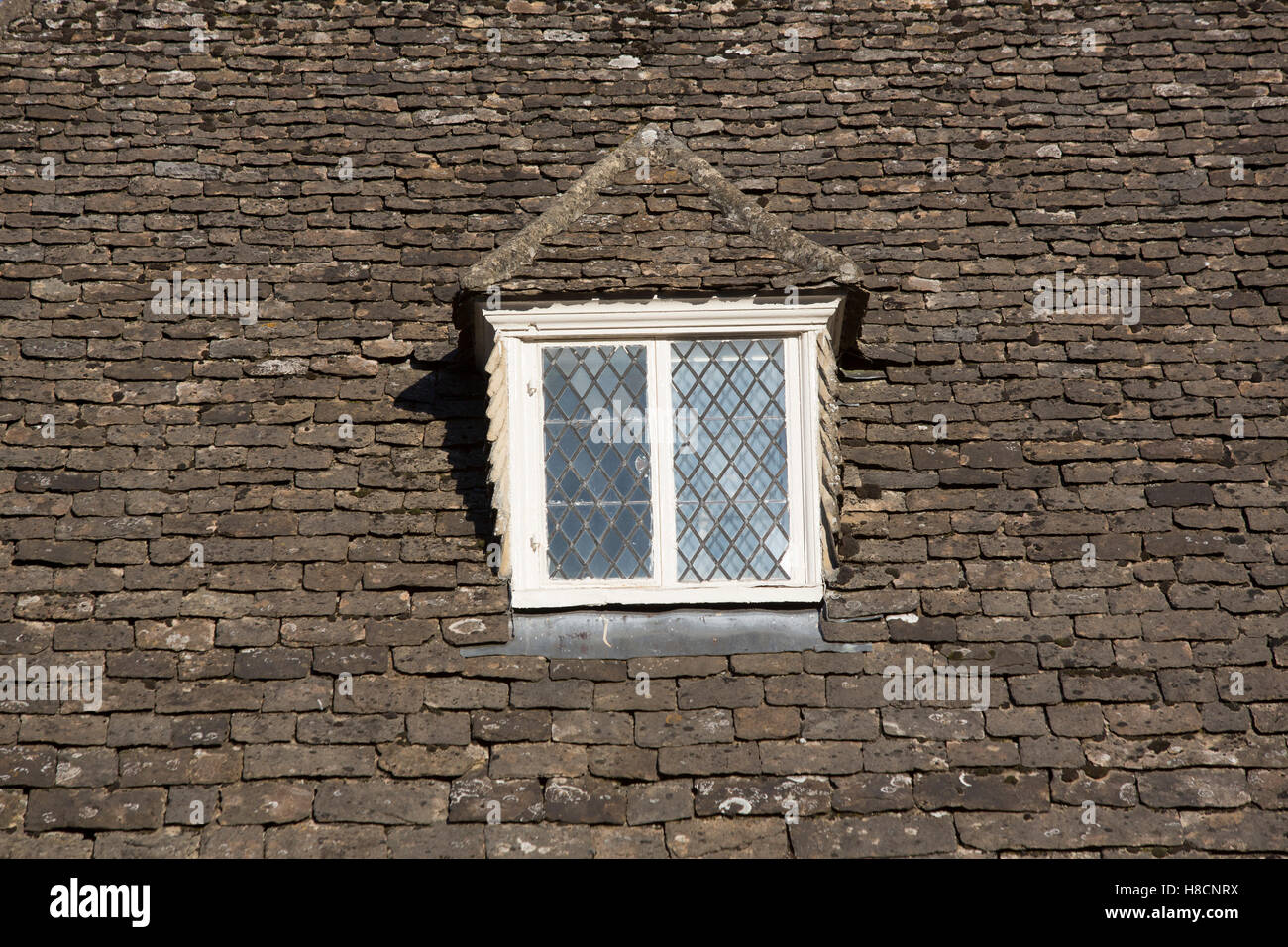 Old weathered tiles on a house roof with a loft or attic window set in ...