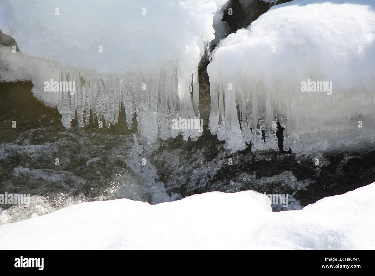 Icicles over a flowing river Stock Photo - Alamy