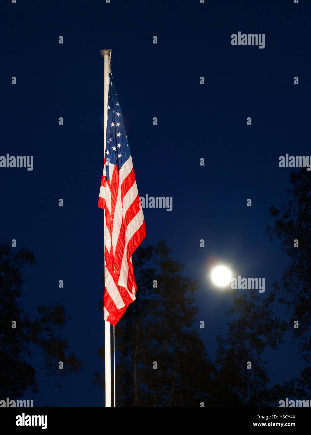 American flag lit up as a full moon rises in the background Stock Photo ...
