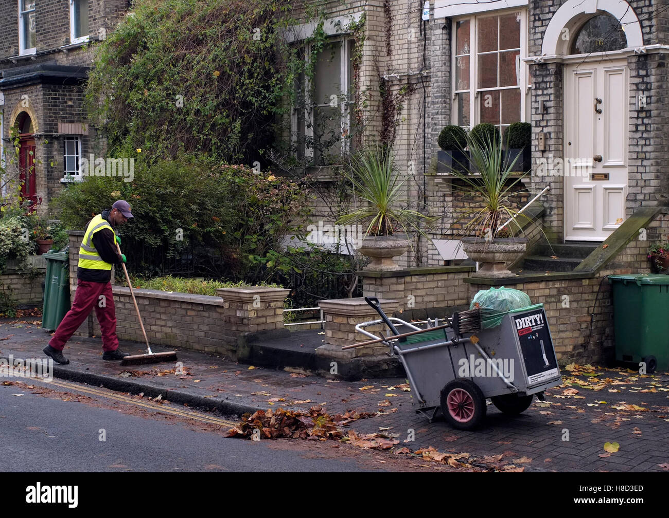 A street cleaner sweeps up leaves in a residential street in Hampstead ...