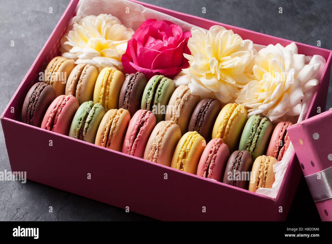 Colorful macaroons and flowers on stone table. Sweet macarons in gift ...