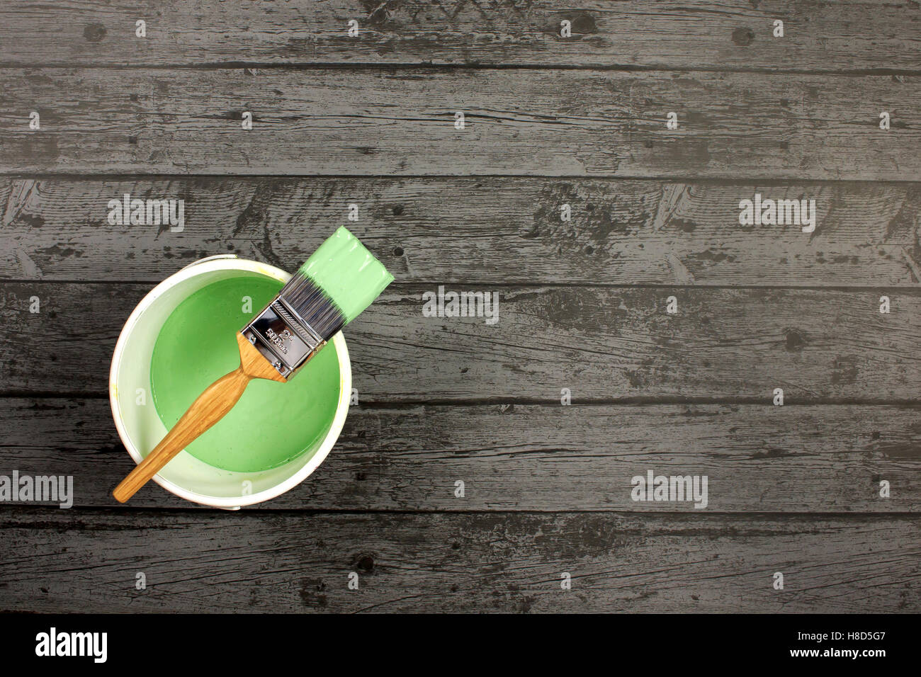 Loaded paintbrush placed across a white paint kettle filled with green ...