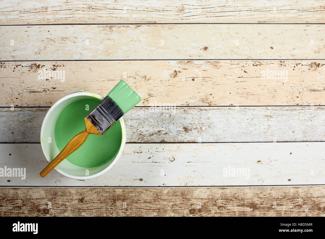 loaded paintbrush placed across a white paint kettle filled with green ...
