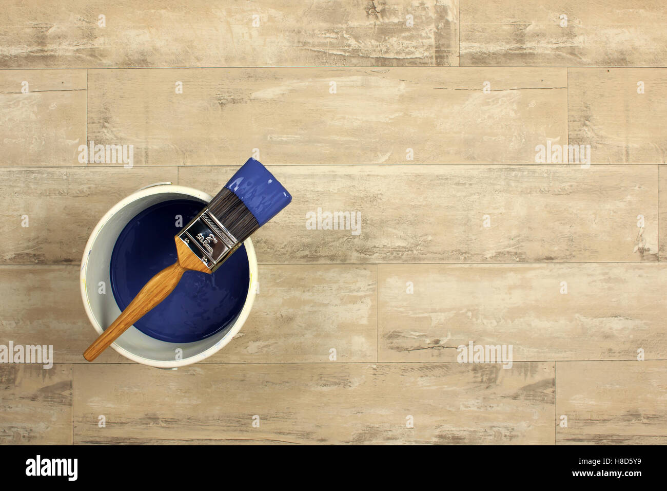 Loaded paintbrush placed across a white paint kettle filled with dark ...