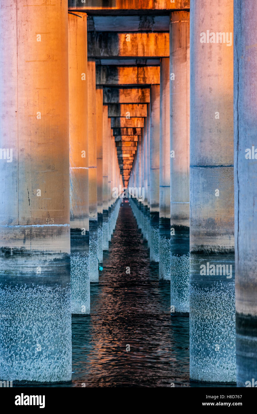 Sunset between columns that form the base of a bridge on the sea Stock ...