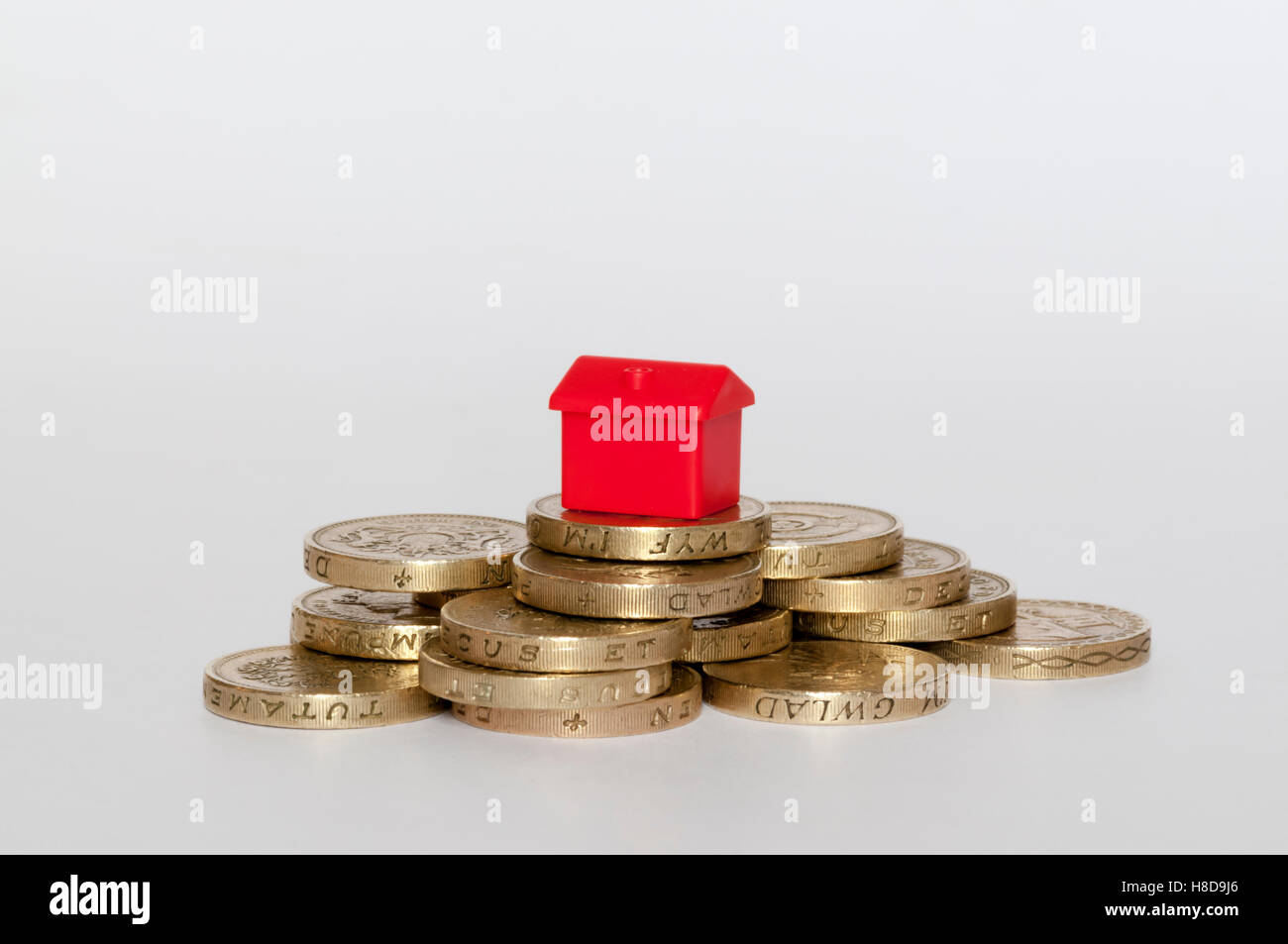 A small plastic model red house on top of a pile of pound coins ...