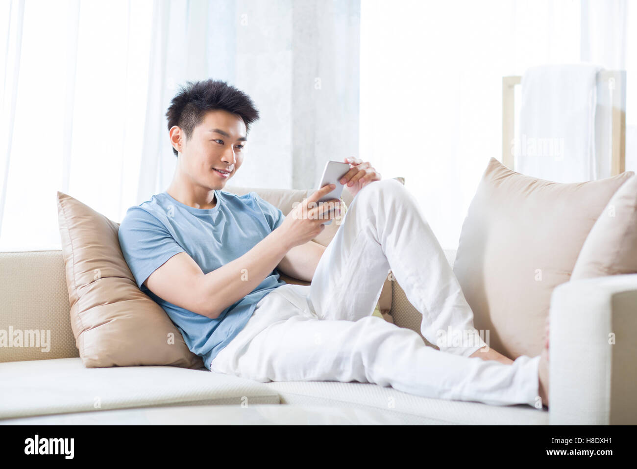 Young Chinese man using smart phone on the sofa Stock Photo - Alamy