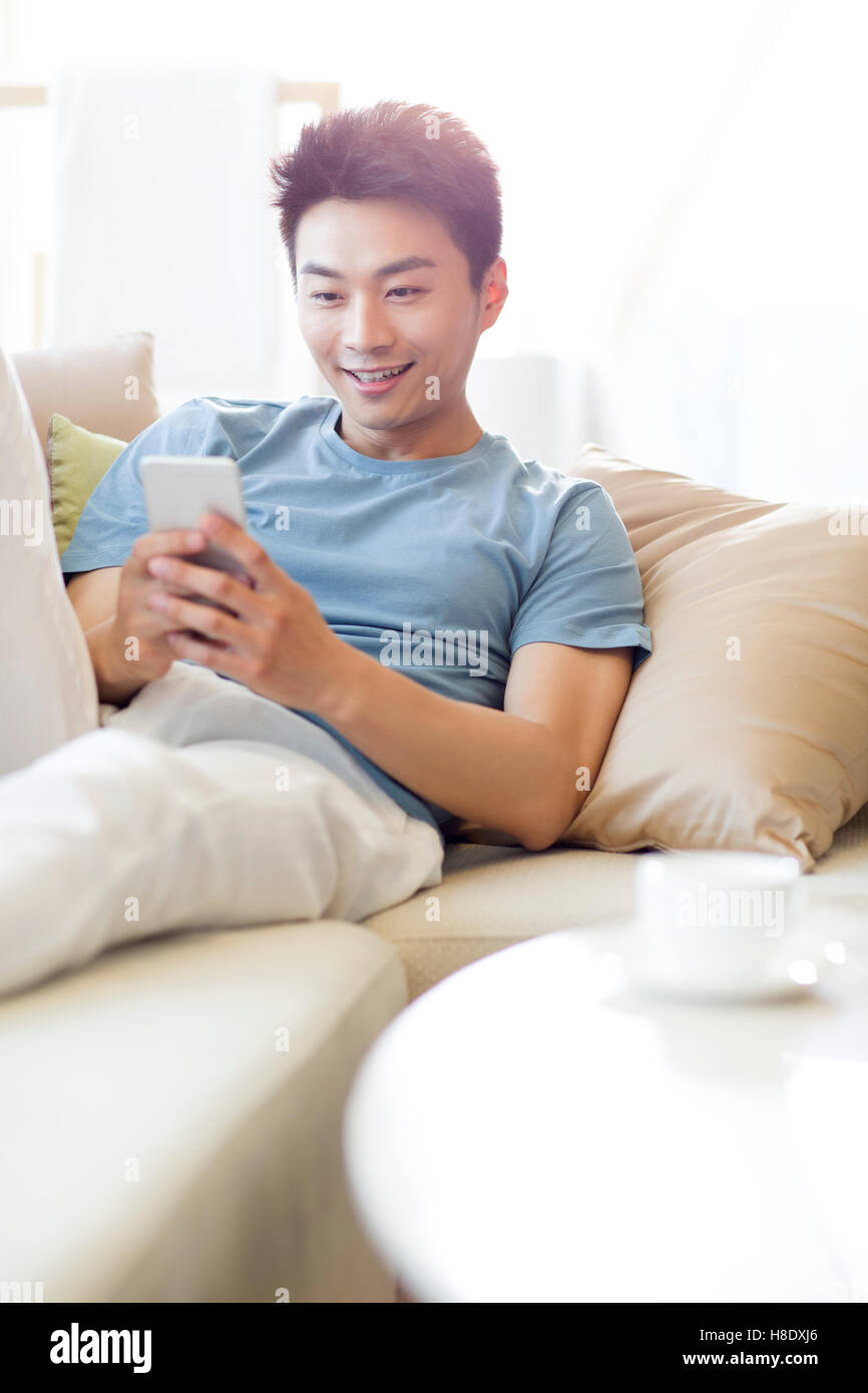 Young Chinese man using smart phone on the sofa Stock Photo - Alamy