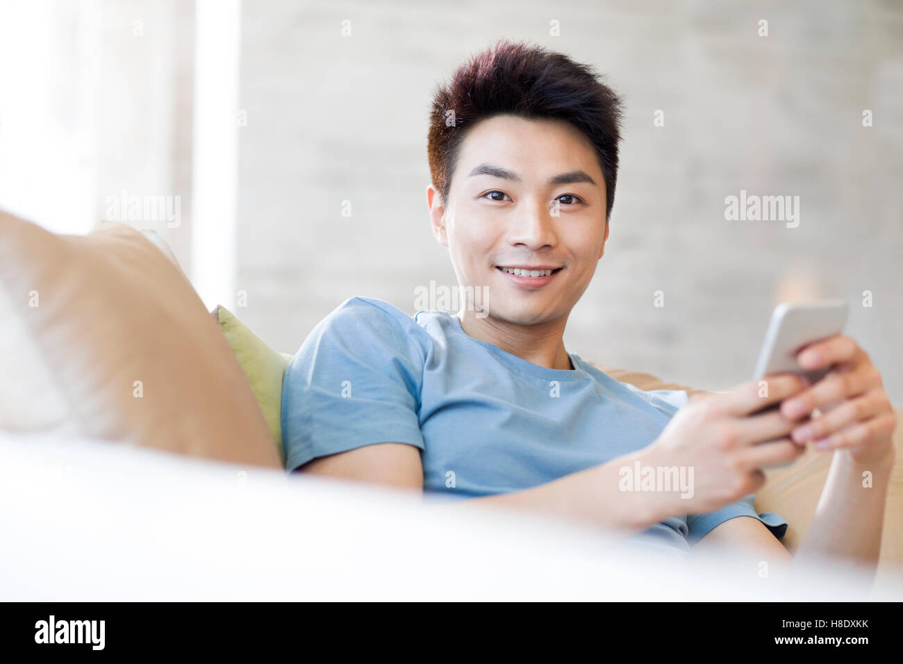 Young Chinese man using smart phone on the sofa Stock Photo - Alamy