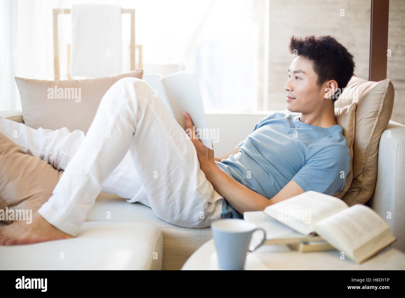 Young Chinese man reading a book on the sofa Stock Photo - Alamy