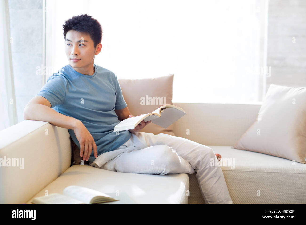 Young Chinese man reading a book on the sofa Stock Photo - Alamy