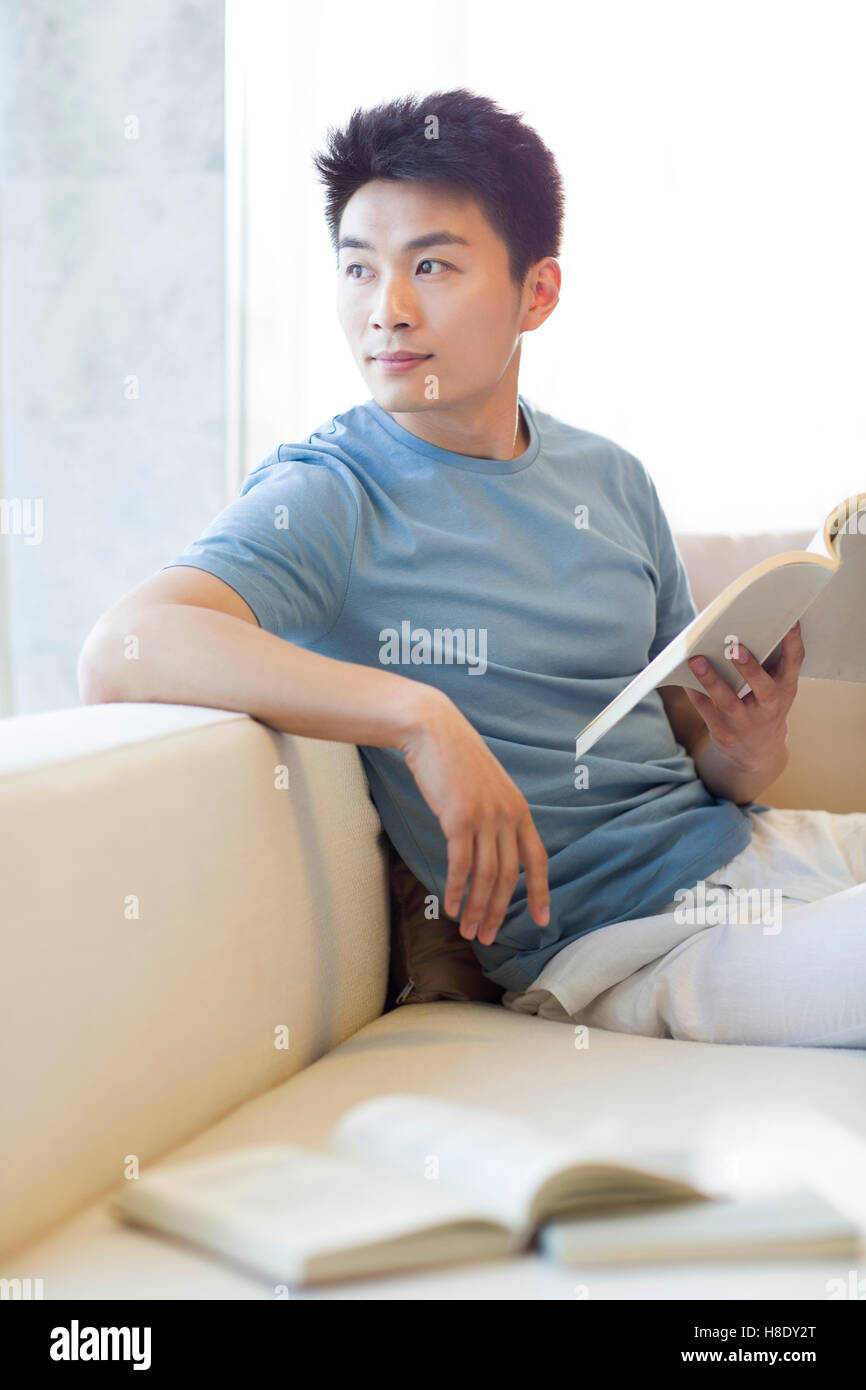 Young Chinese man reading a book on the sofa Stock Photo - Alamy