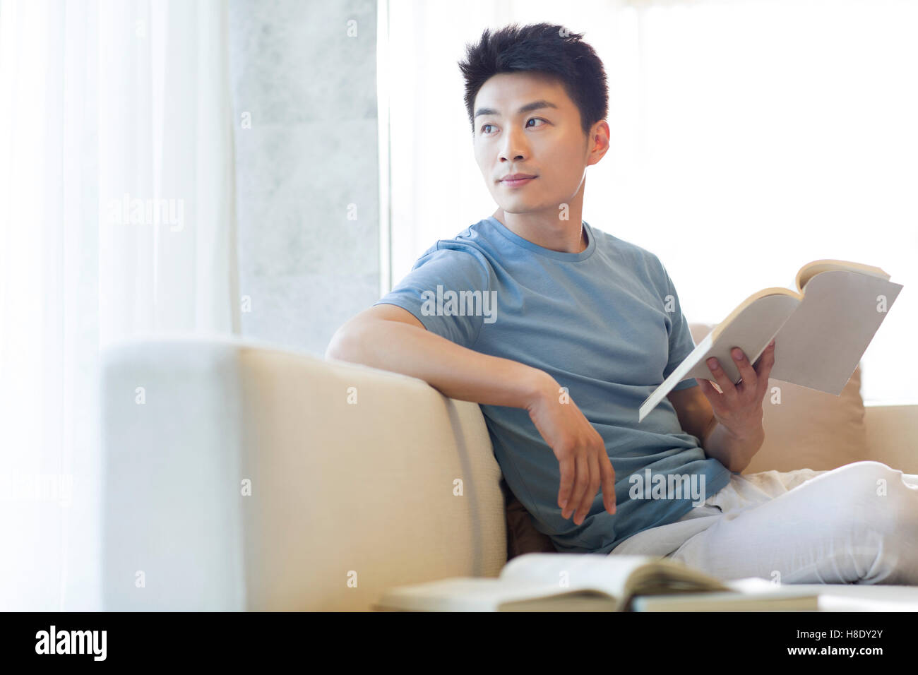 Young Chinese man reading a book on the sofa Stock Photo - Alamy