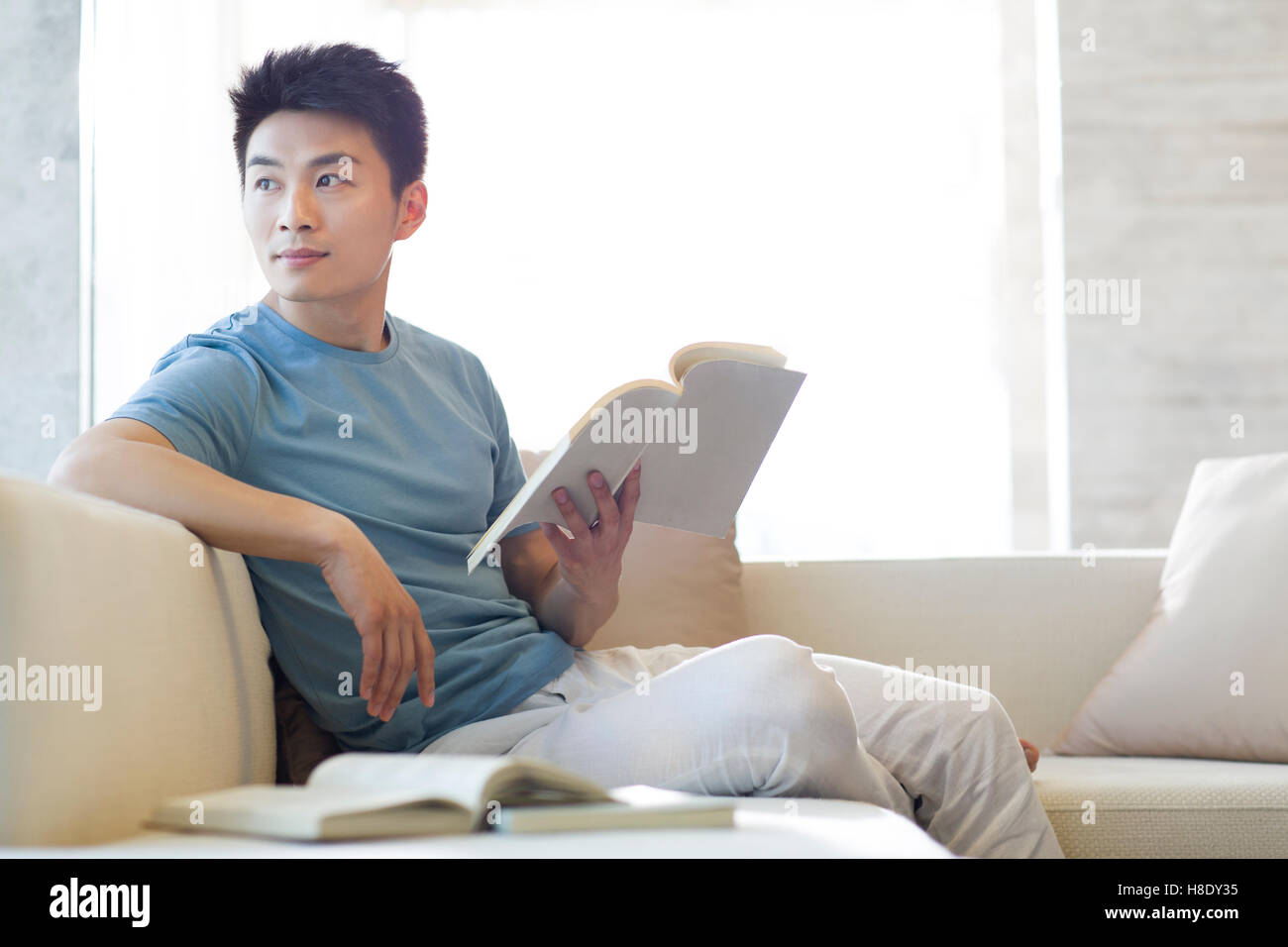 Young Chinese man reading a book on the sofa Stock Photo - Alamy