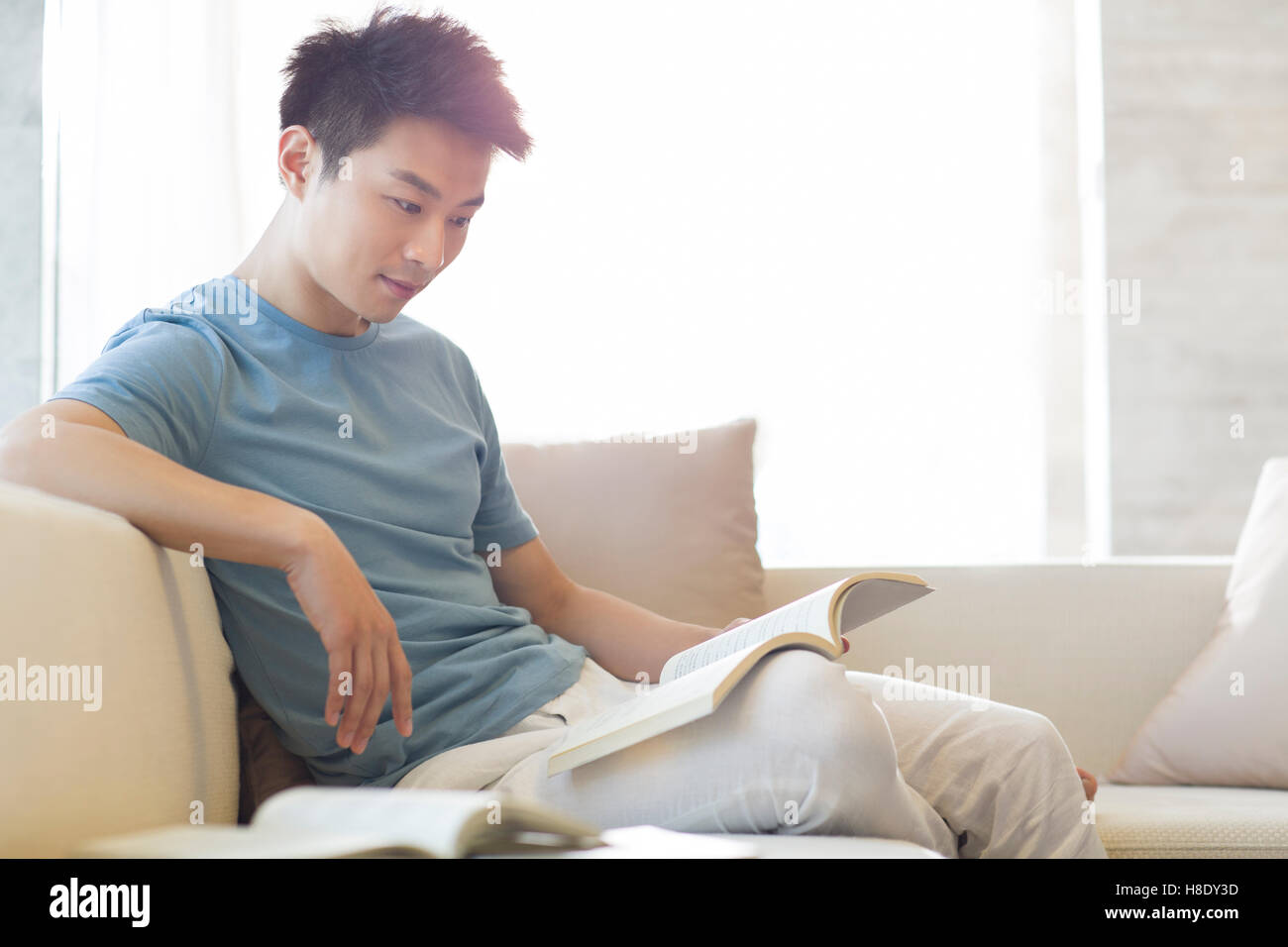Young Chinese man reading a book on the sofa Stock Photo - Alamy