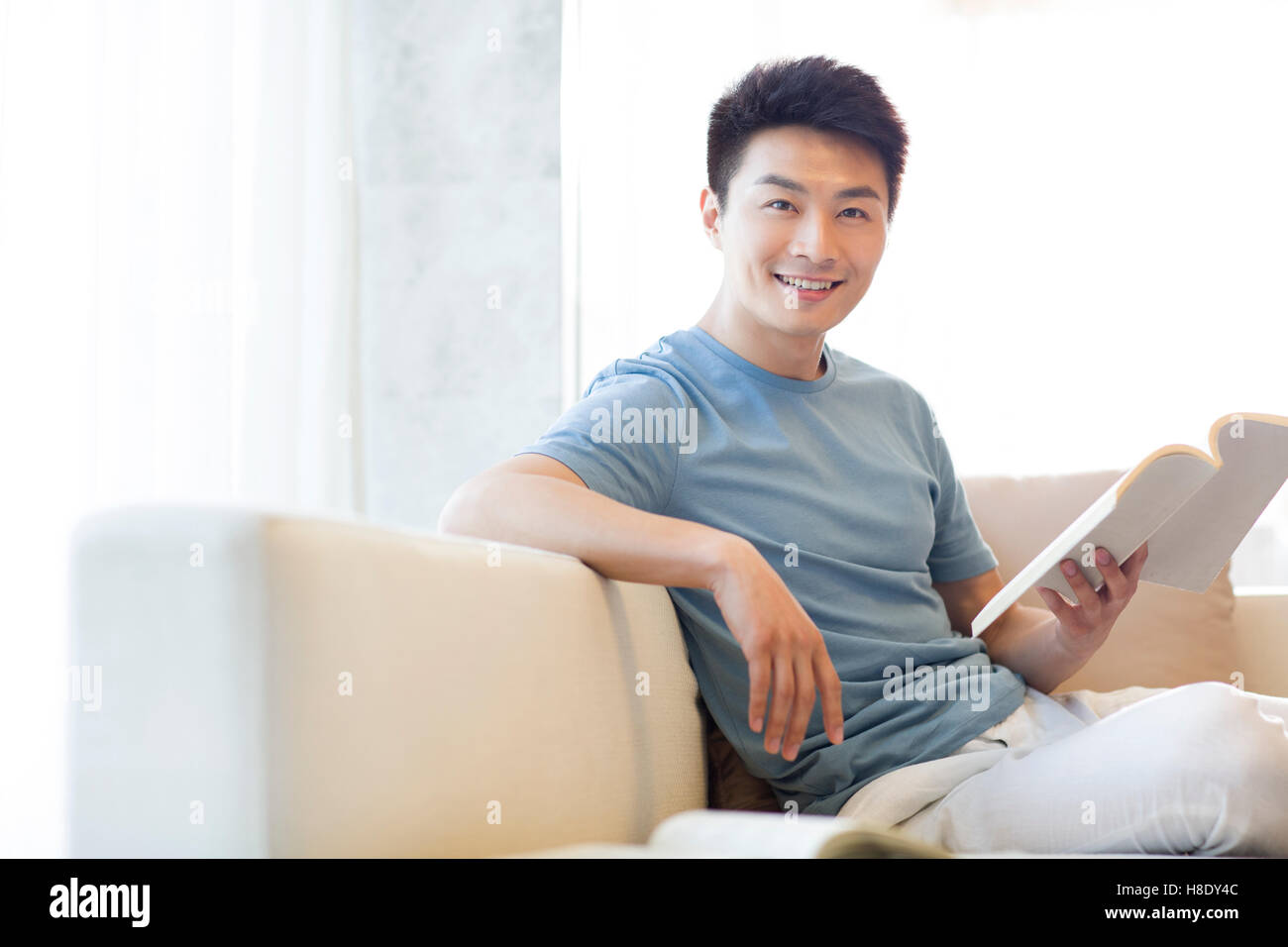 Young Chinese man reading a book on the sofa Stock Photo - Alamy