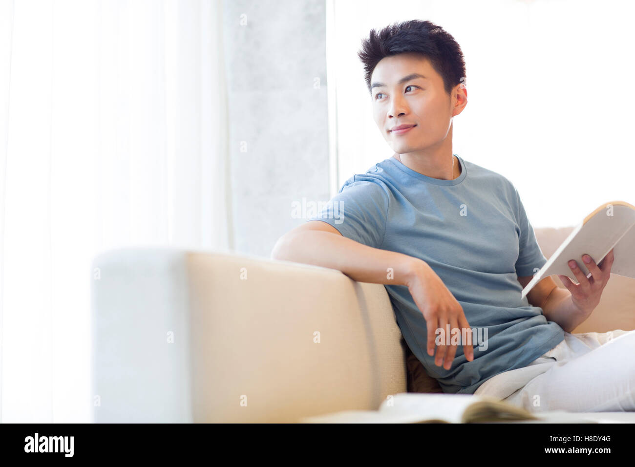 Young Chinese man reading a book on the sofa Stock Photo - Alamy