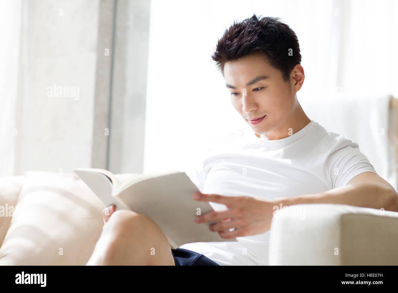 Young Chinese man reading a book on the sofa Stock Photo - Alamy