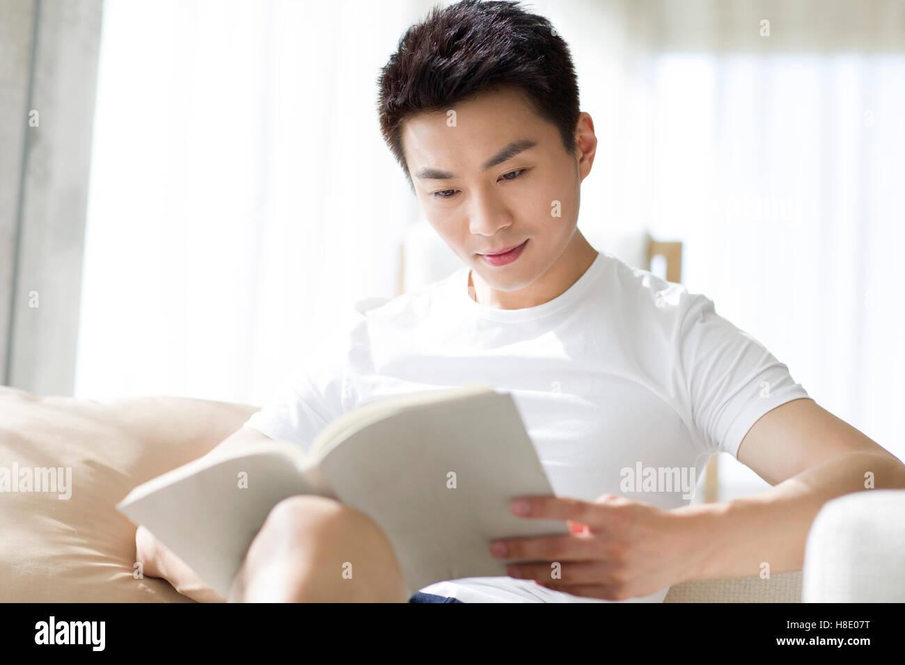 Young Chinese man reading a book on the sofa Stock Photo - Alamy