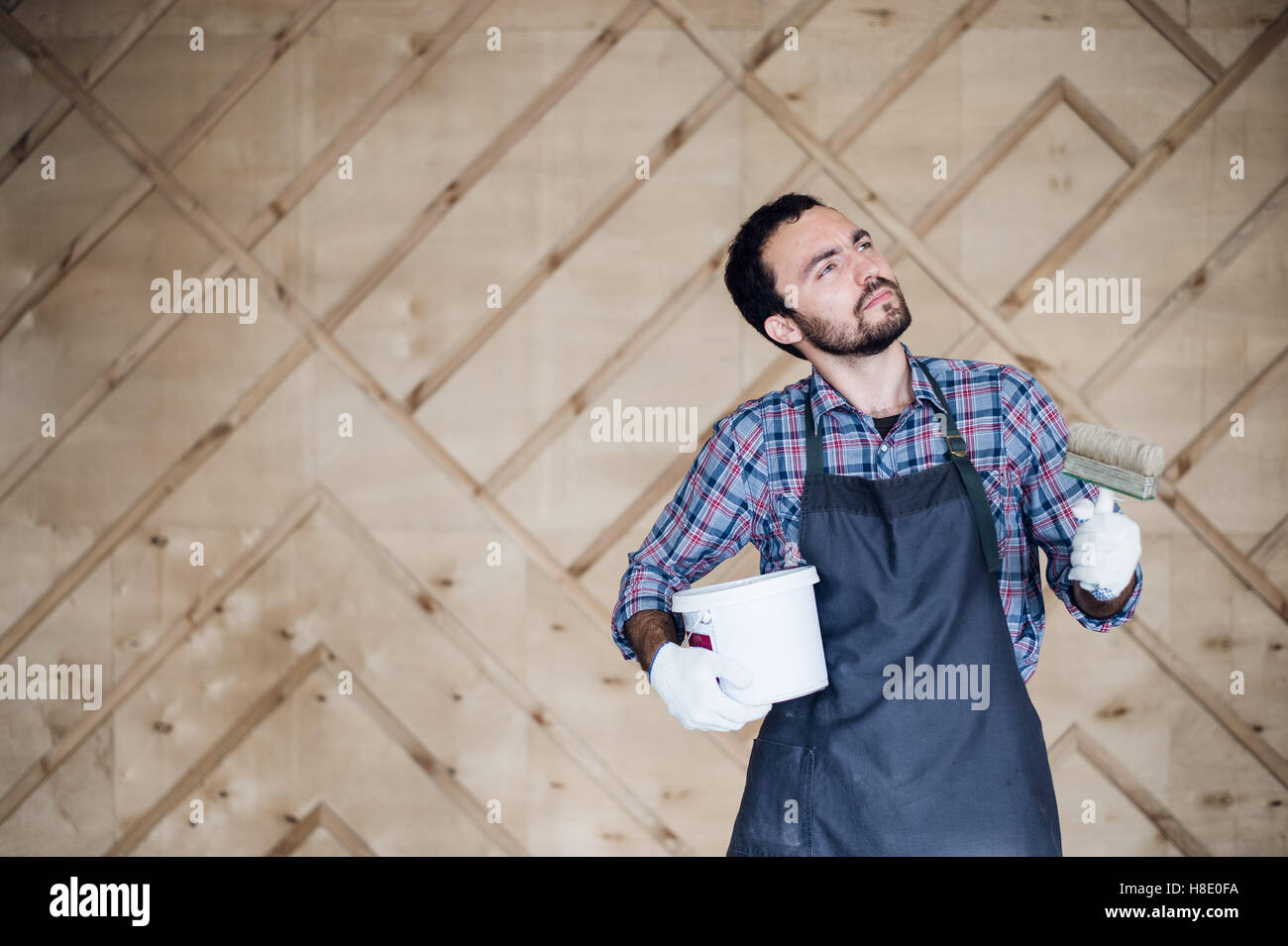 Man with tin of paint and brush looking up on a wooden wall background ...
