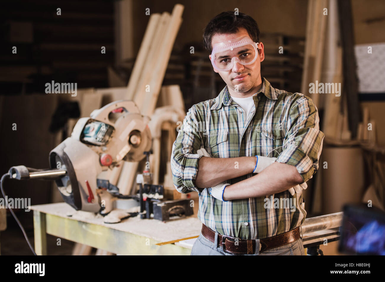 Handsome carpenter in protective glasses is looking at camera and ...