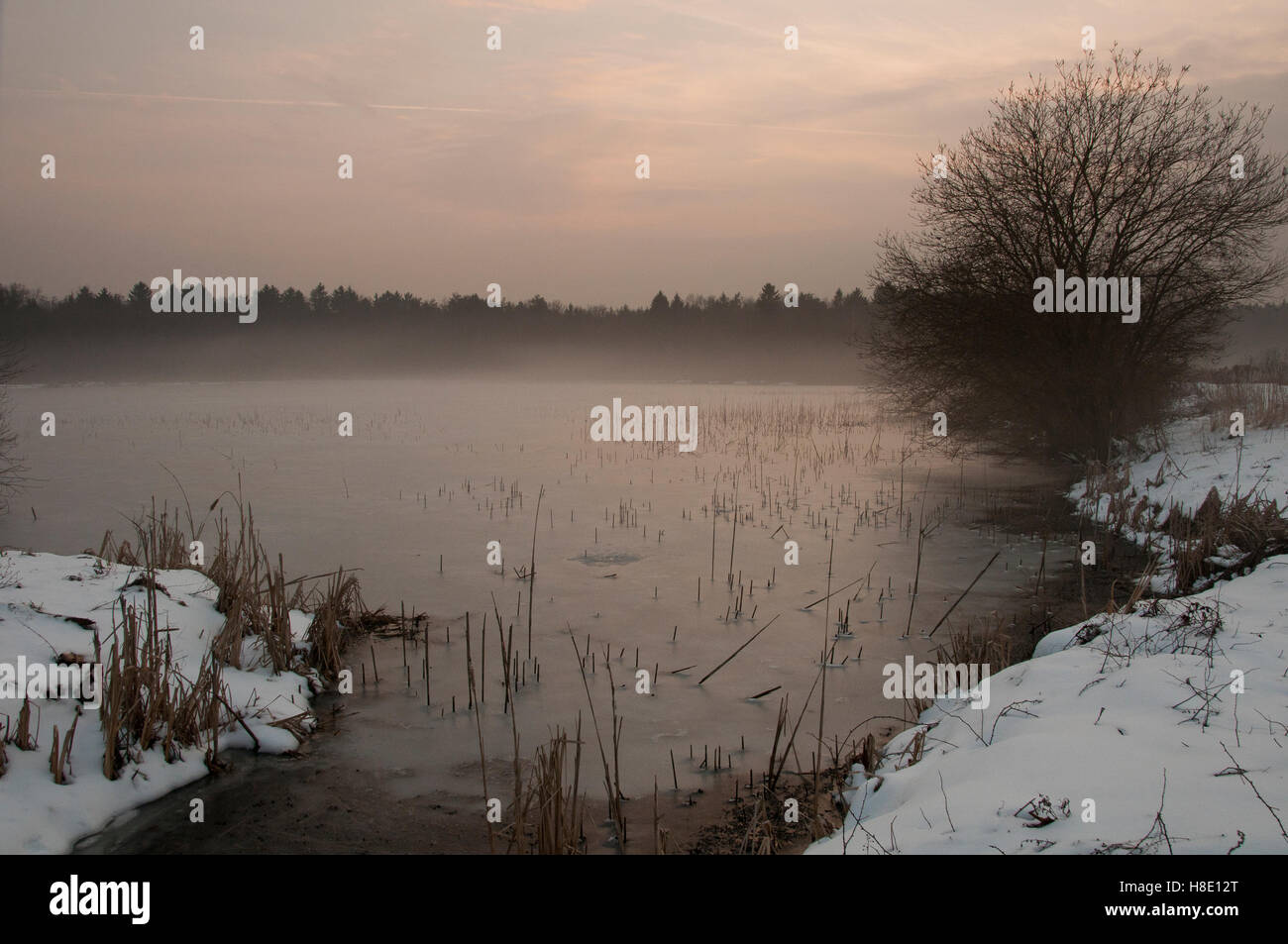 Winter lake covered in ice at sunset while fog rises over the lake, a ...