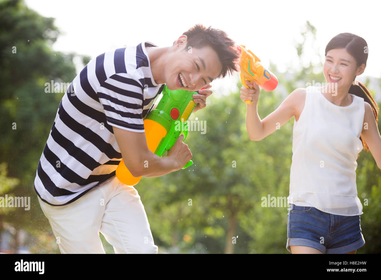 Happy young Chinese couple playing squirt guns Stock Photo - Alamy