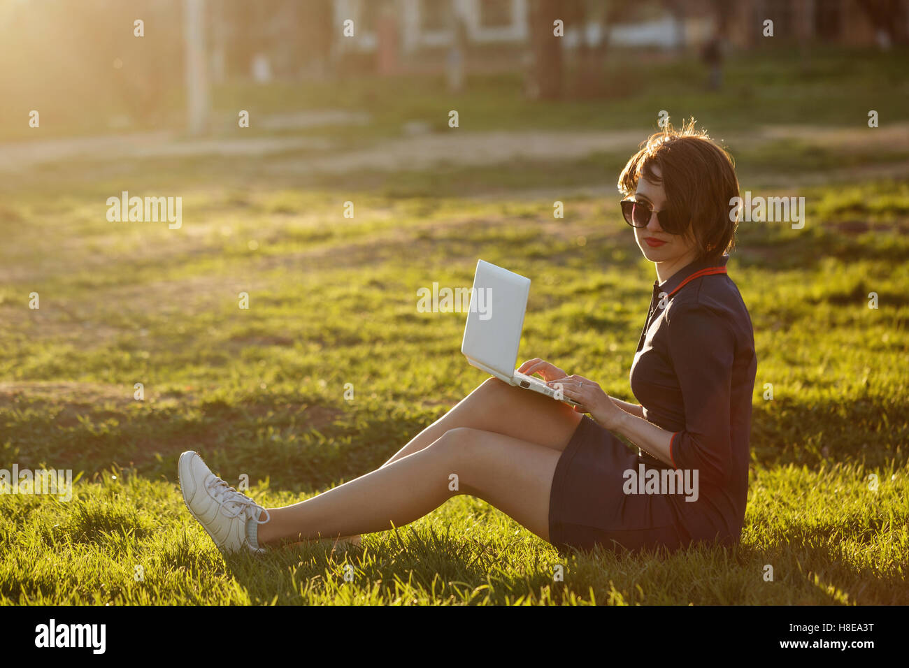 Cute girl sitting on the lawn in the park. Student works with a laptop. Wireless Internet ...