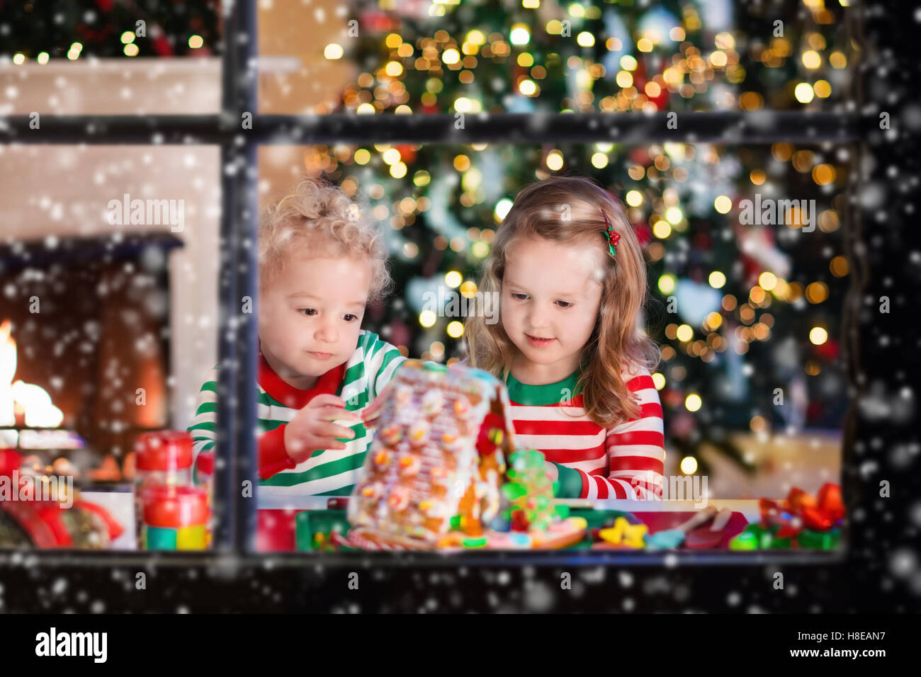 Little boy and girl making Christmas gingerbread house at fireplace in ...