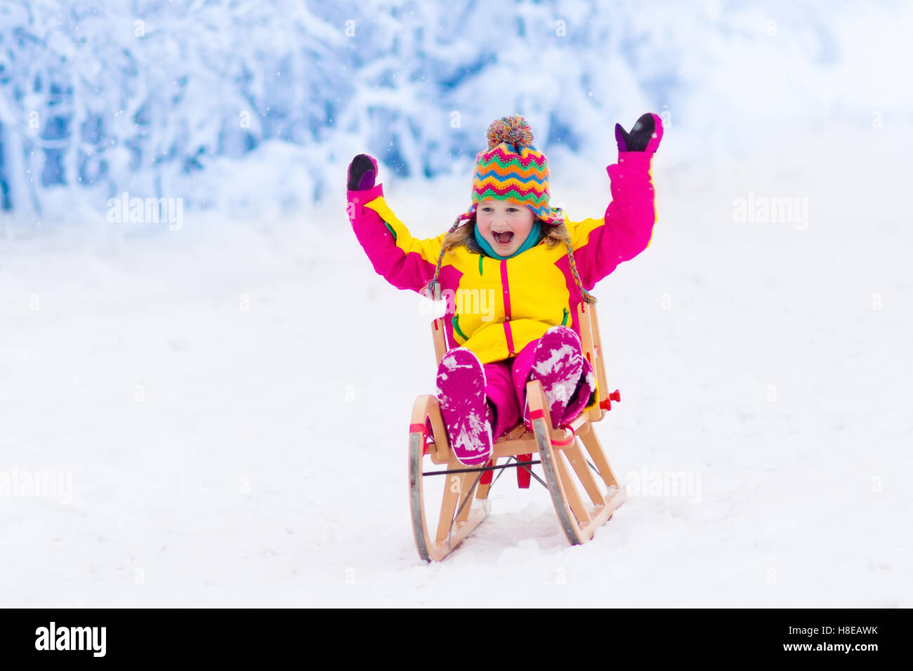 Little girl enjoying sleigh ride. Child sledding. Toddler kid riding a sledge. Children play ...